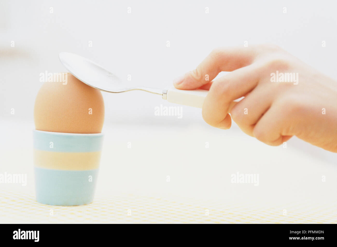 Spoon tapping boiled egg in an eggcup, side view Stock Photo - Alamy