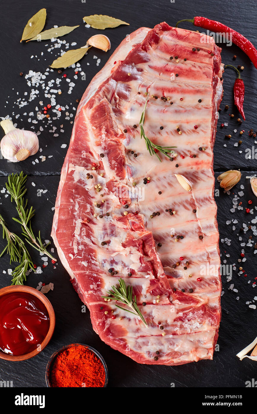 rack of raw pork spare ribs seasoned with spices on black slate tray ...