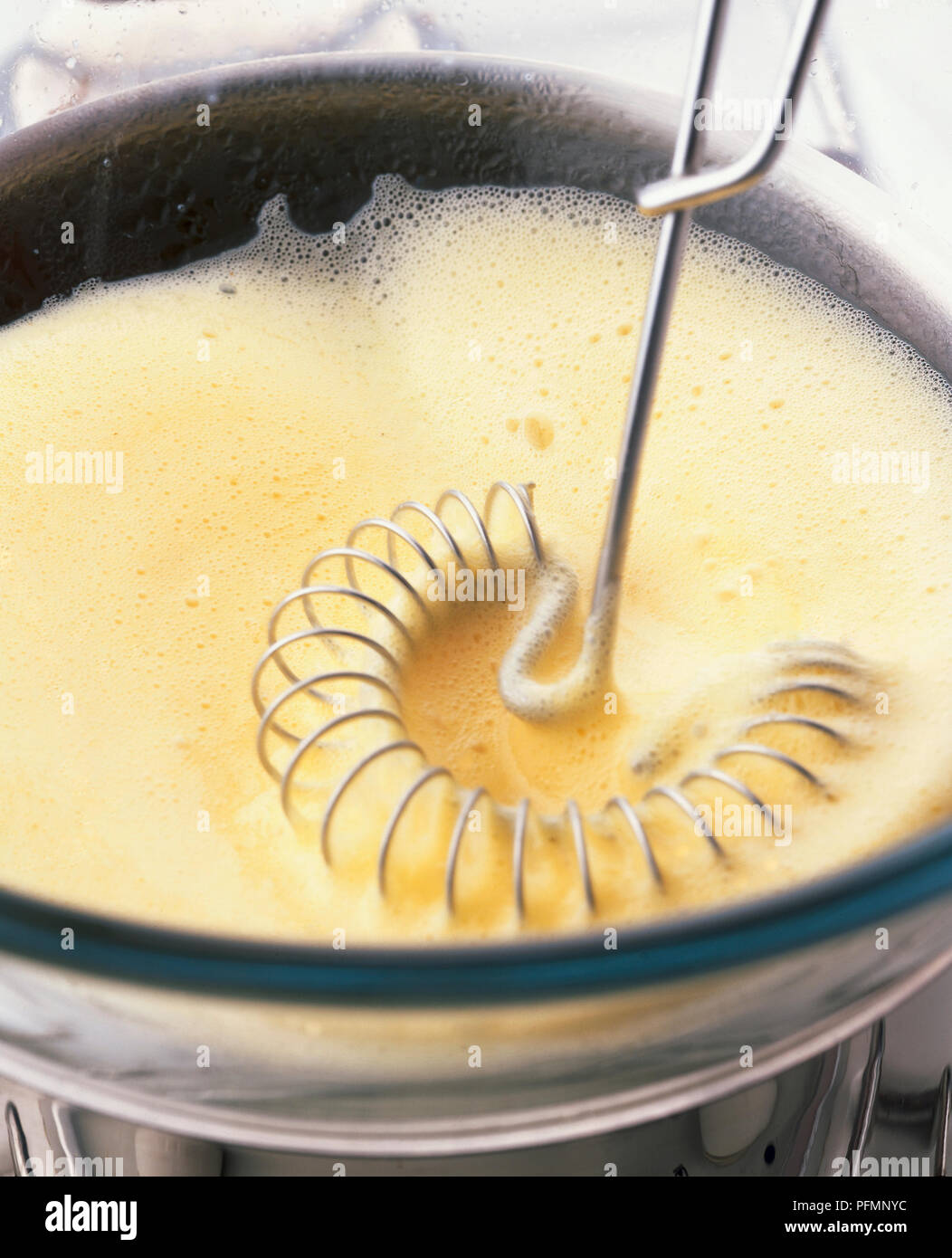Simmering hollandaise mixture being whisked with a flat-coiled wire ...