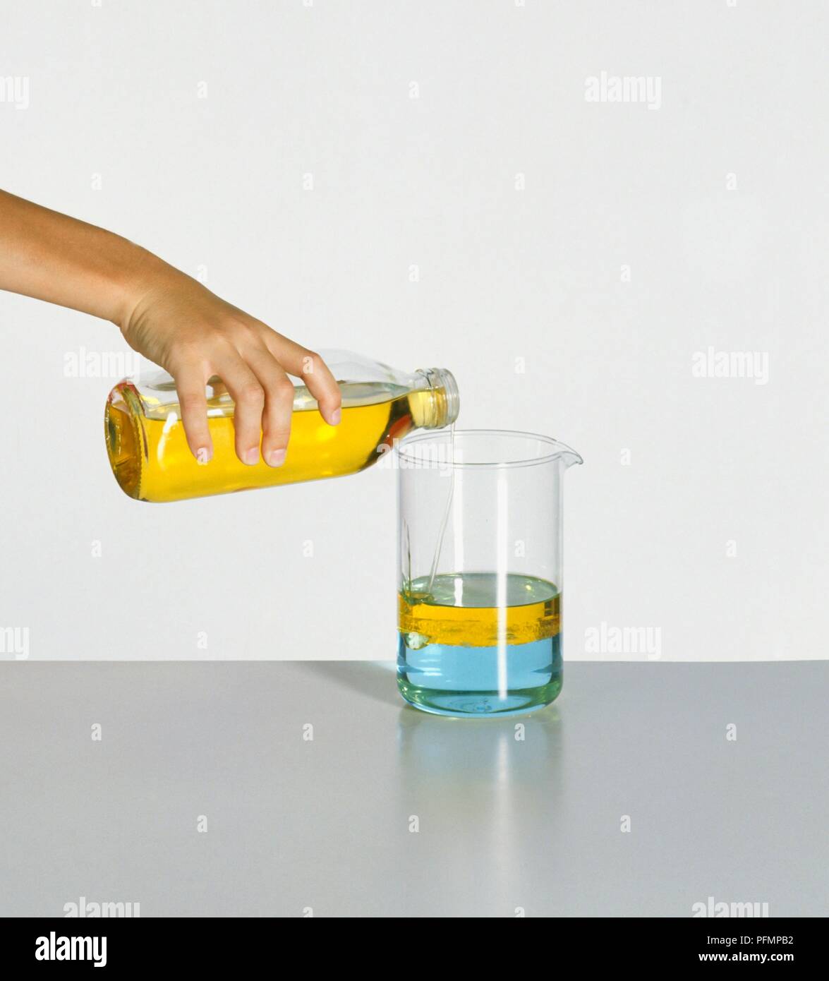 Hand pouring cooking oil over water in beaker Stock Photo - Alamy