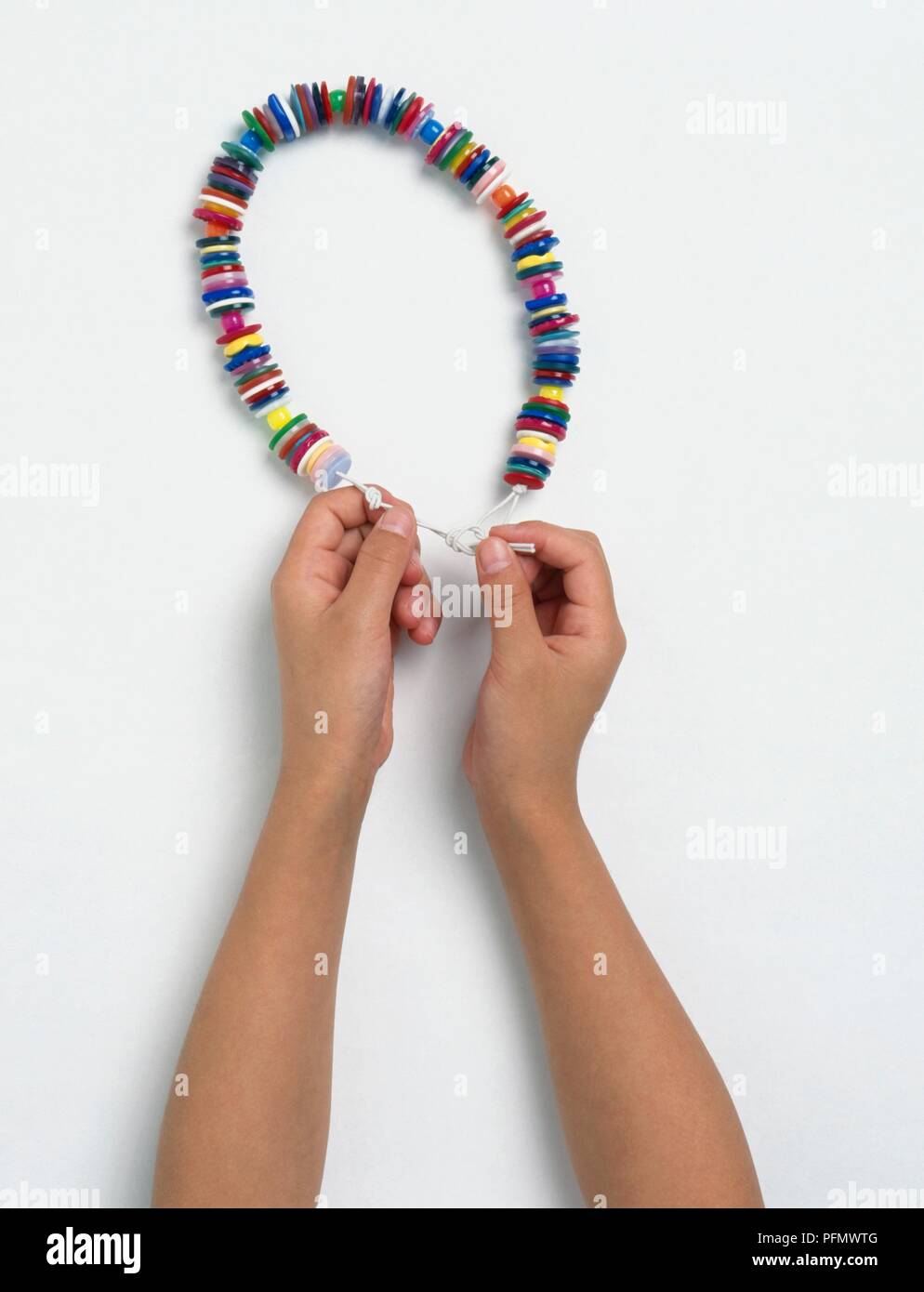 Girl tying loose ends of elastic thread together of button necklace ...