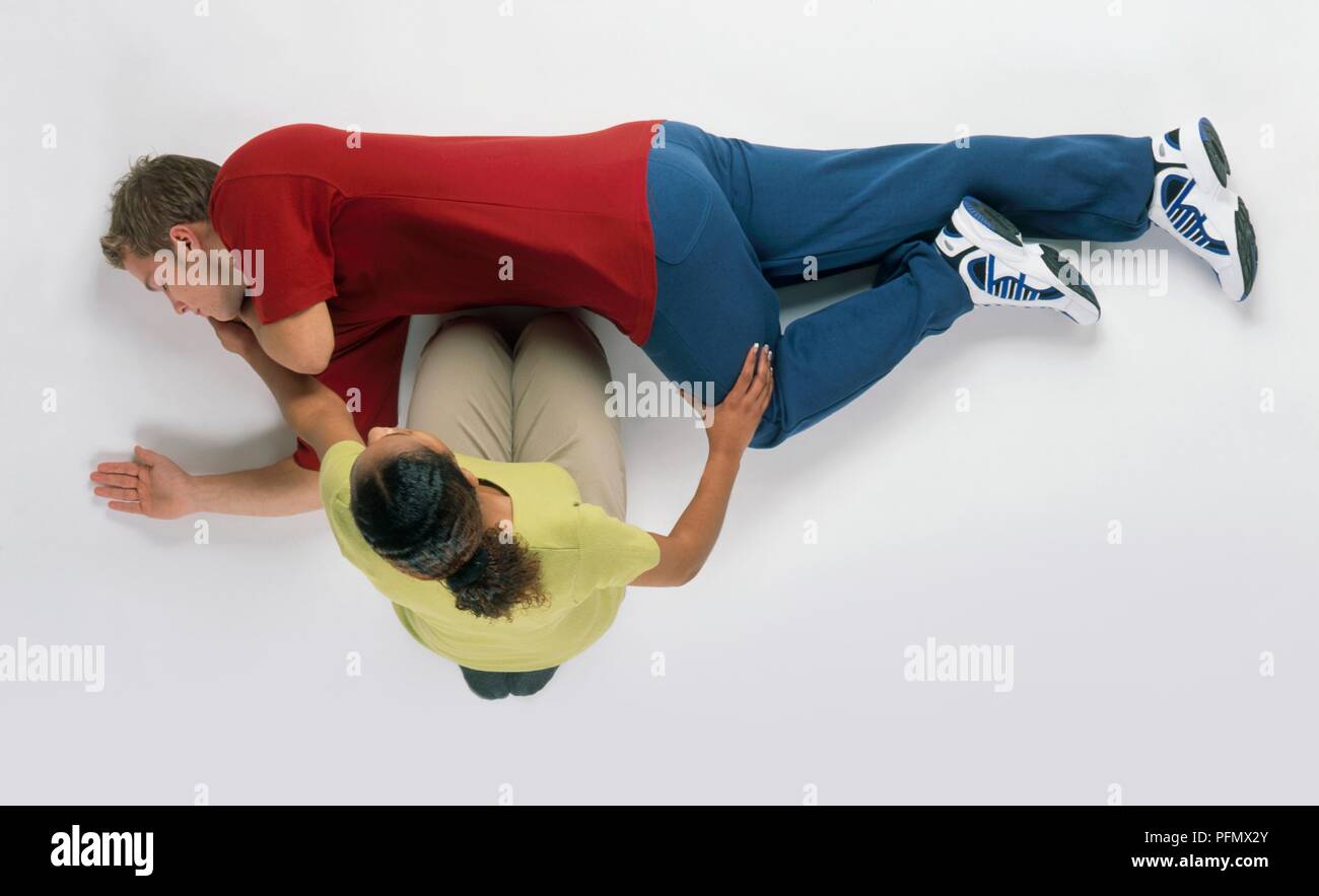 Man in recovery position, woman kneeling beside holding his knee and ...