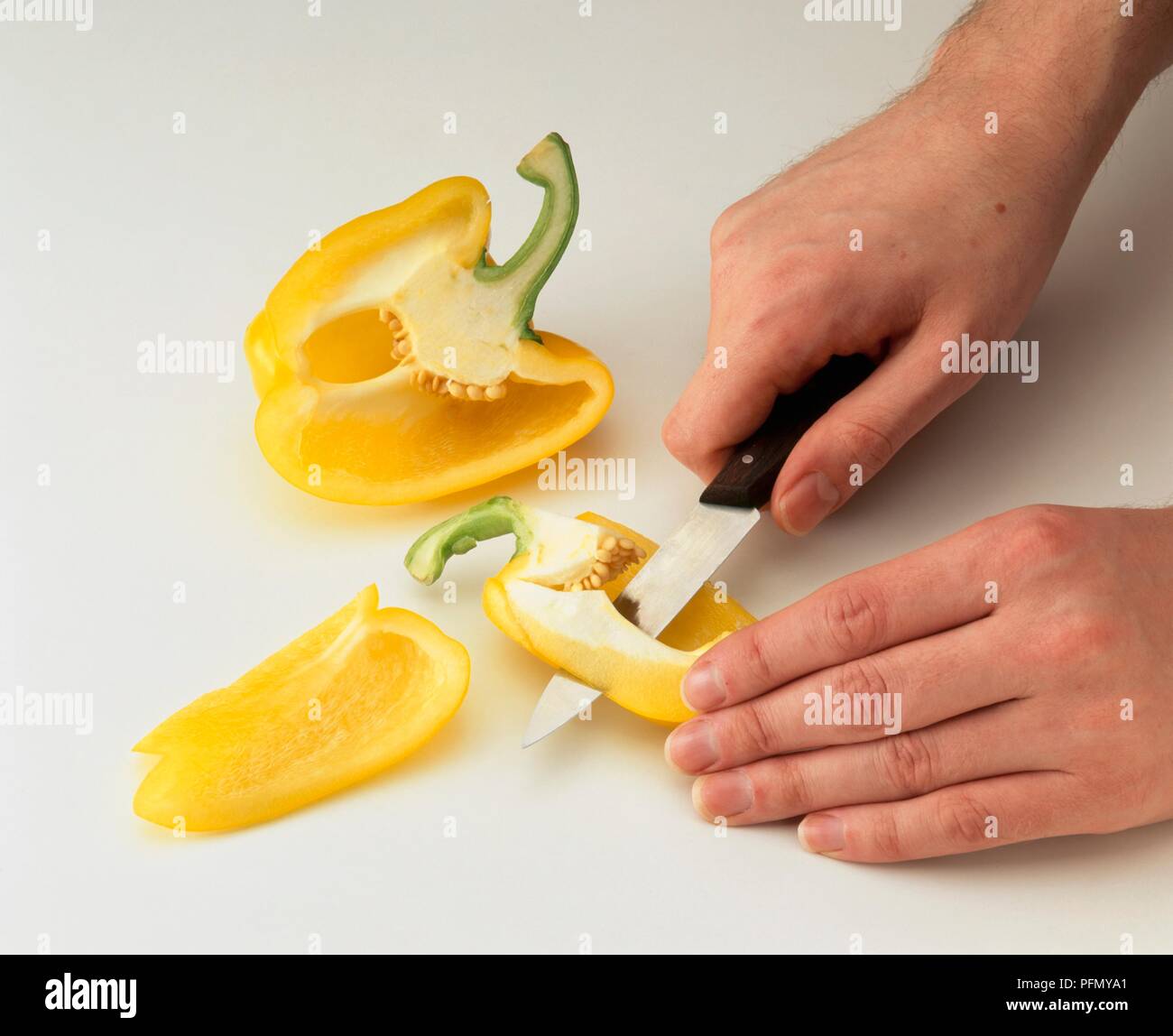 Using small kitchen knife to cut core and seeds from yellow bell pepper ...