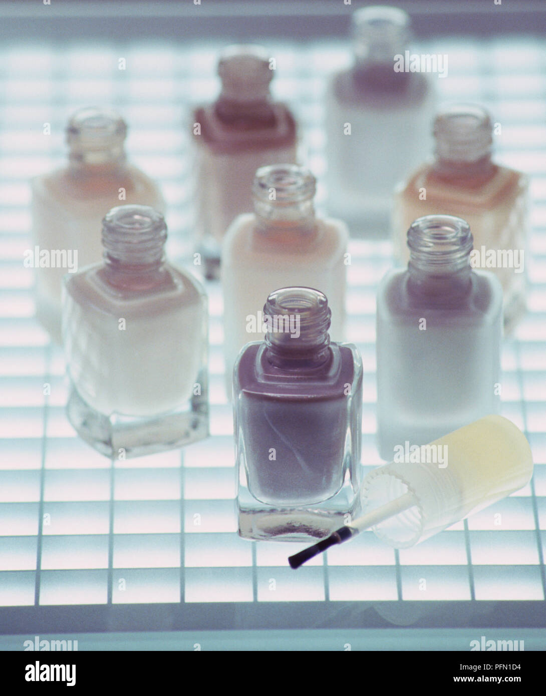 Bottles containing various pale shades of nail polish with their lids ...