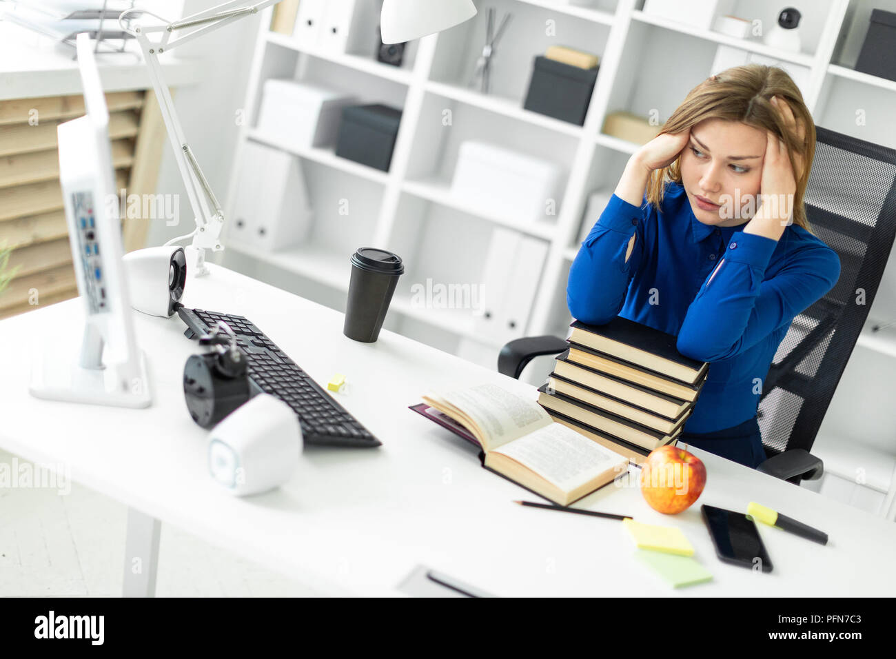 A young girl sits at a computer desk and holds her hands behind her ...