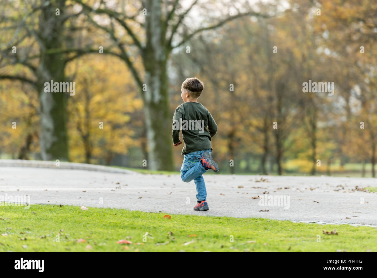 Side rear view of young boy running on road in autumn park Stock Photo ...