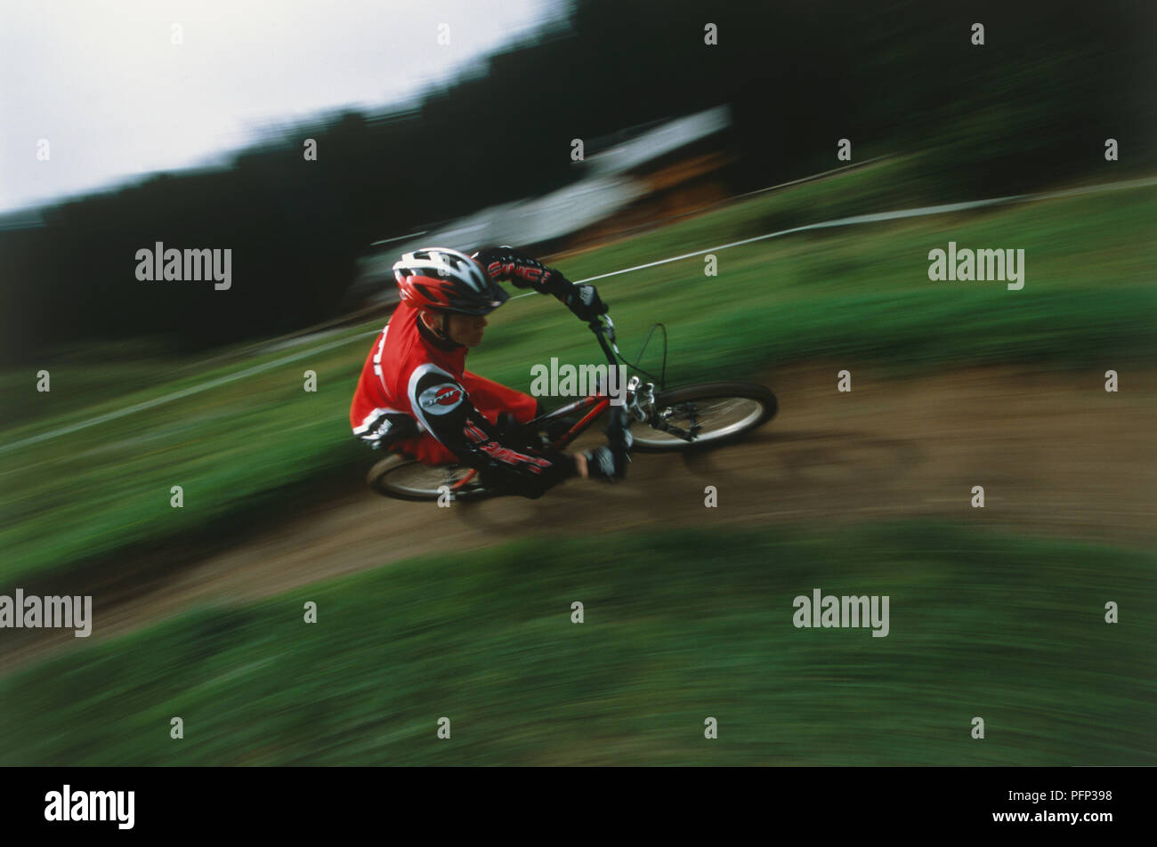 Male cyclist in red outfit riding along dirt track, motion blurring ...