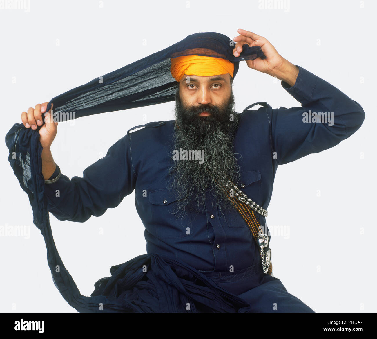 Man wrapping dark blue turban around his head over an orange base ...