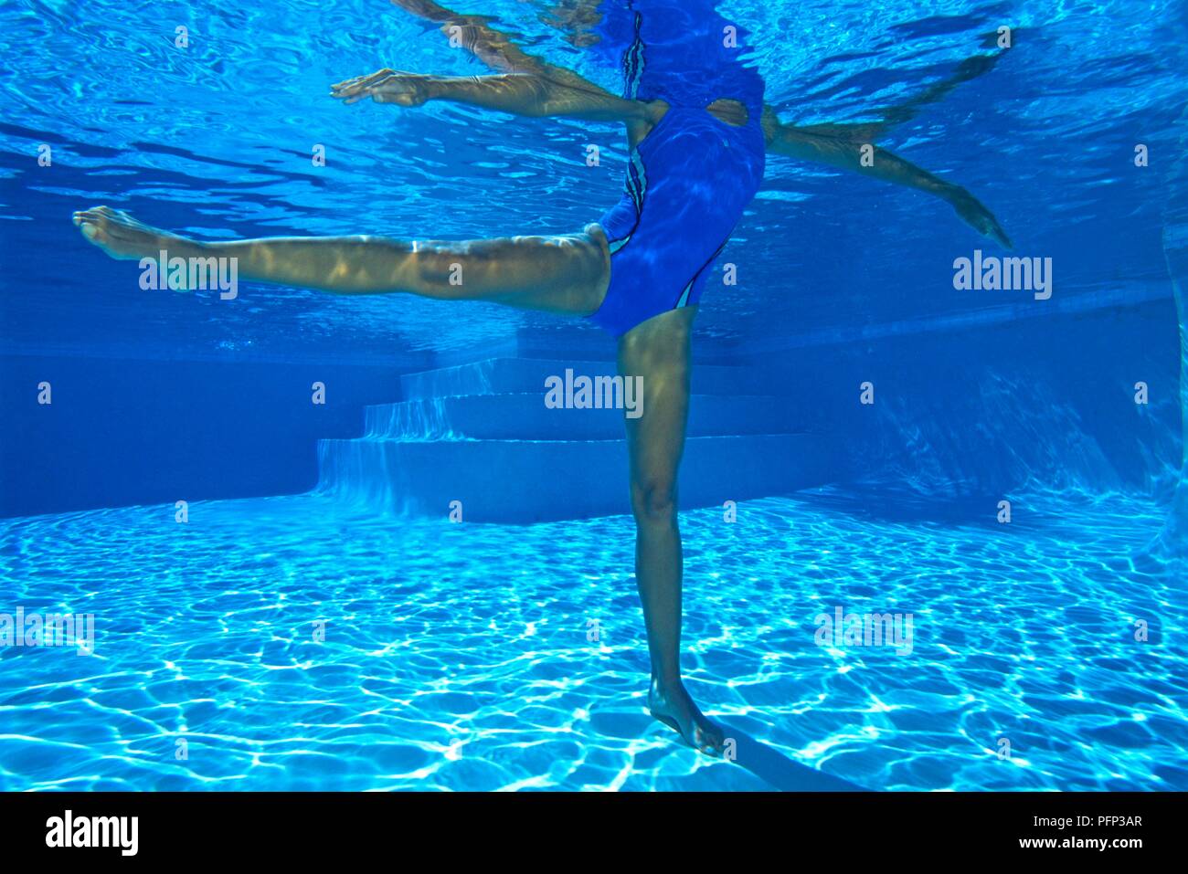 Woman wearing bathing suit, underwater, standing on one leg, kicking ... Woman wearing bathing suit, underwater, standing on one leg, kicking ...