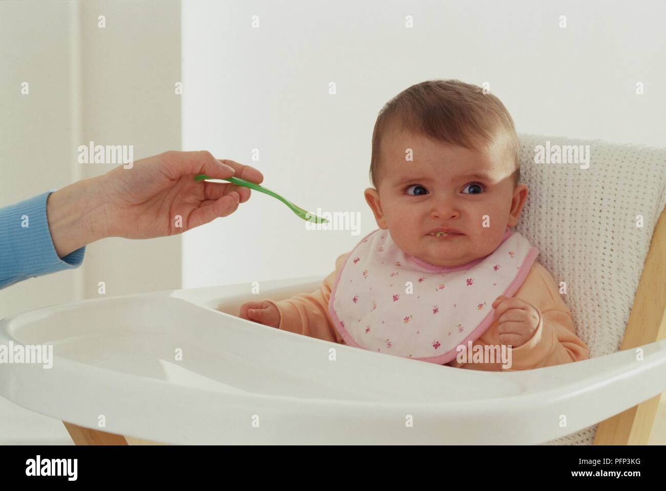 Baby in high chair turning head away from food on spoon Stock Photo - Alamy