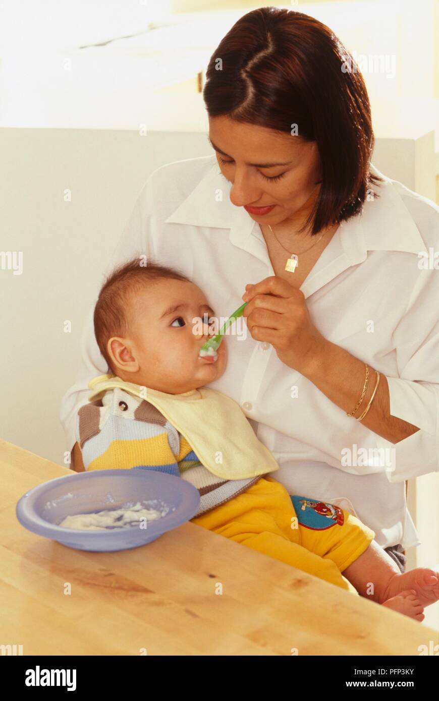 Woman supporting baby boy on her arm, holding green spoon to baby's ...