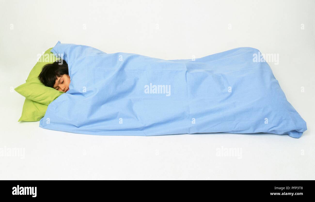 Boy lying in bed covered with blue duvet Stock Photo - Alamy