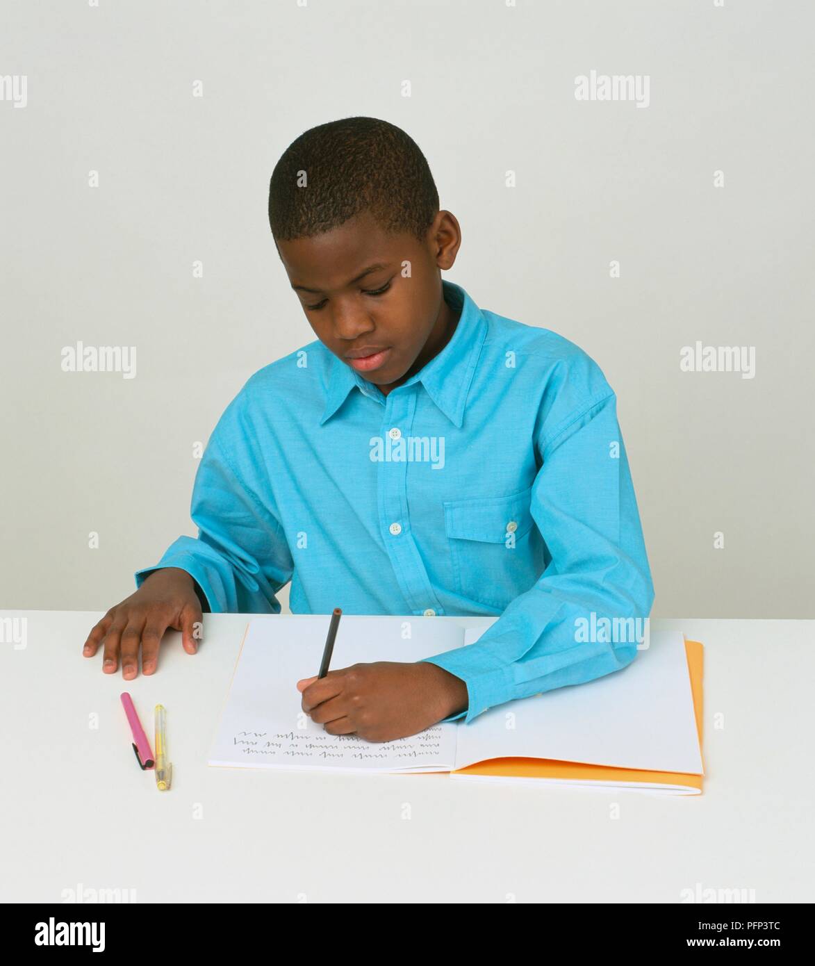 Boy in blue shirt writing in exercise book on desk Stock Photo - Alamy