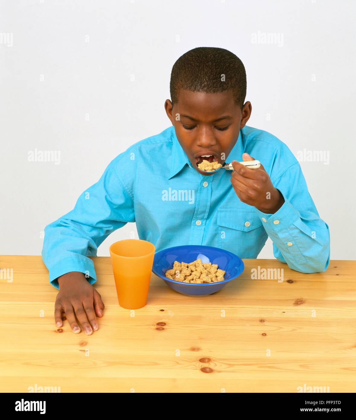 Boy in blue shirt eating breakfast cereals from bowl, cup nearby Stock ...