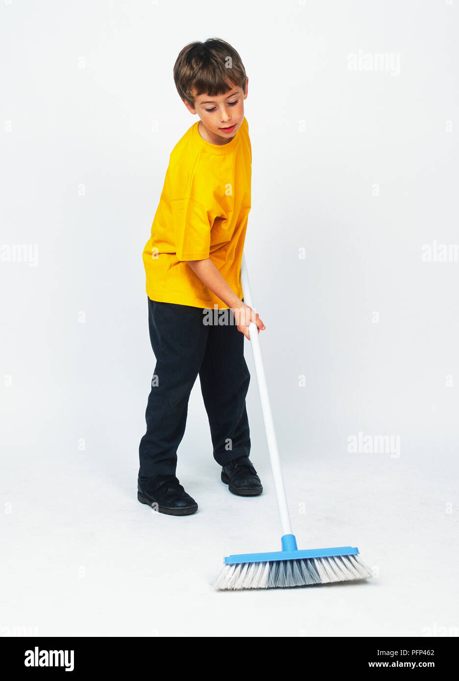 Boy in yellow T-shirt and black trousers sweeping the floor, front view ...