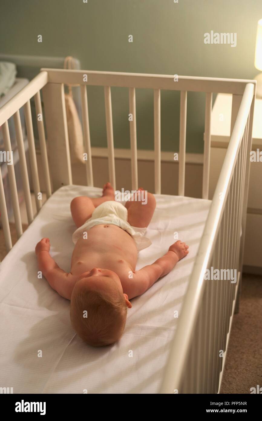 Baby with nappy on lying on his back in cot Stock Photo - Alamy