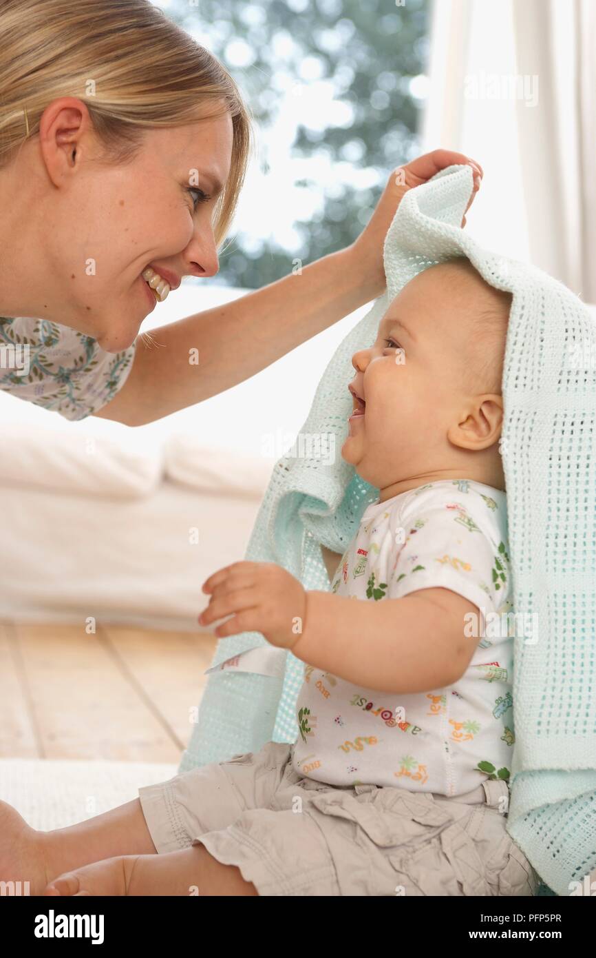 Baby boy sitting covered with a blanket, woman lifting top of blanket ...