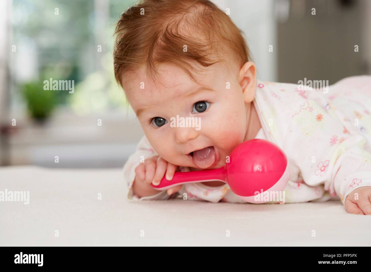 Baby girl lying on front holding rattle Stock Photo - Alamy