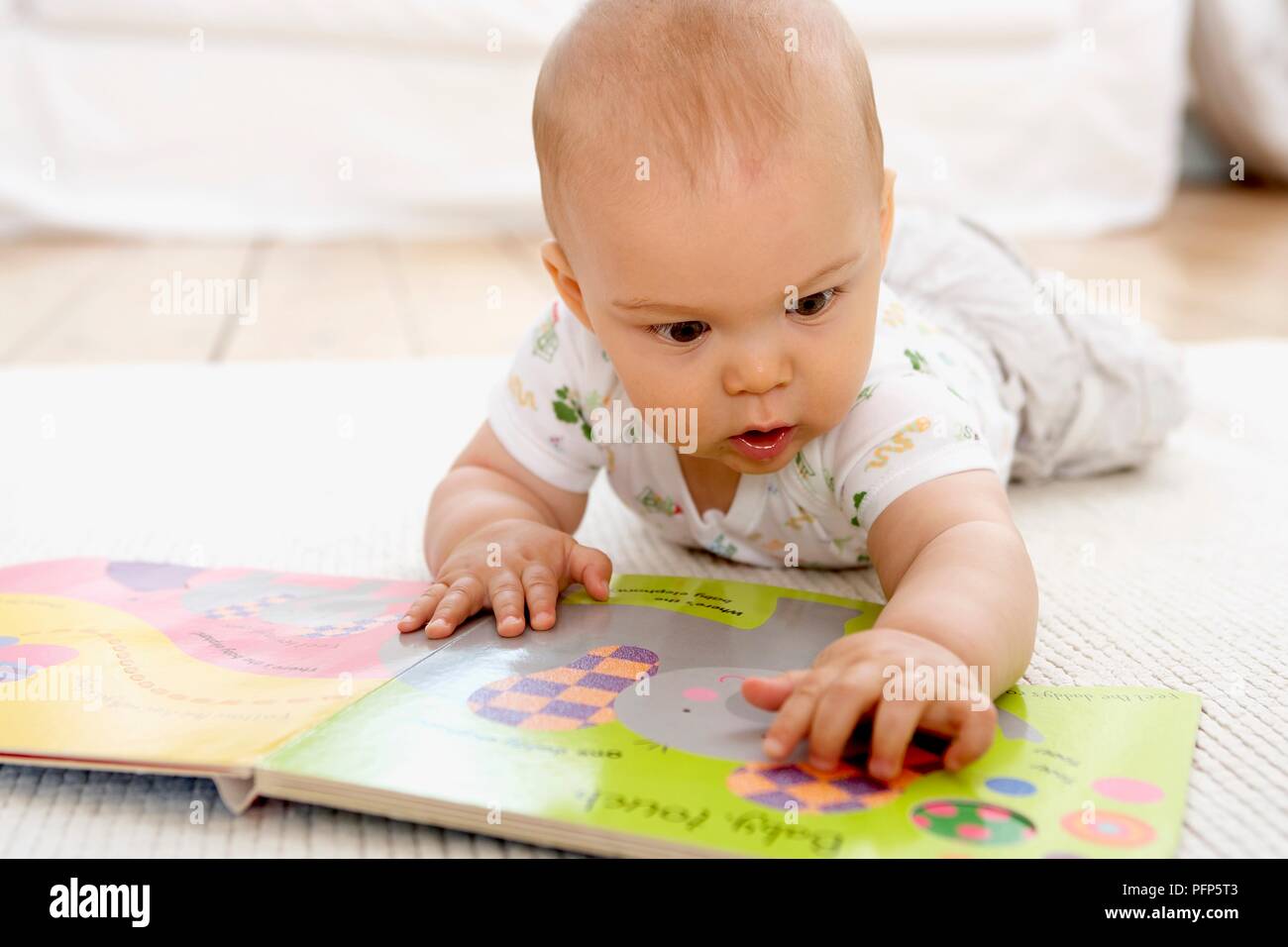 Baby boy lying on floor with picture book, touching page with his hands ...