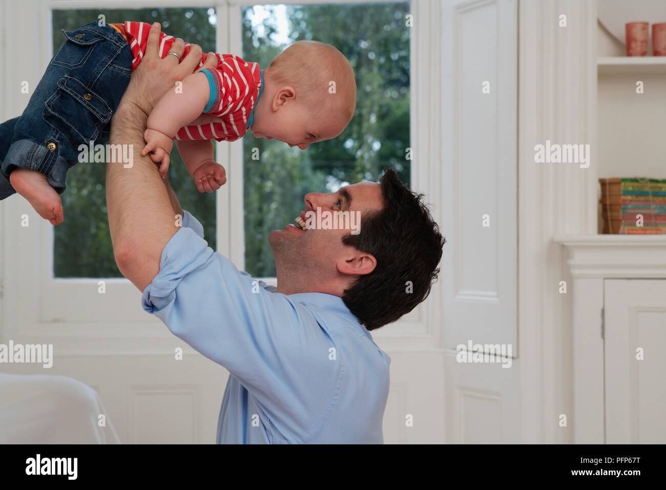 Man holding a baby boy aloft, both smiling, side view Stock Photo - Alamy