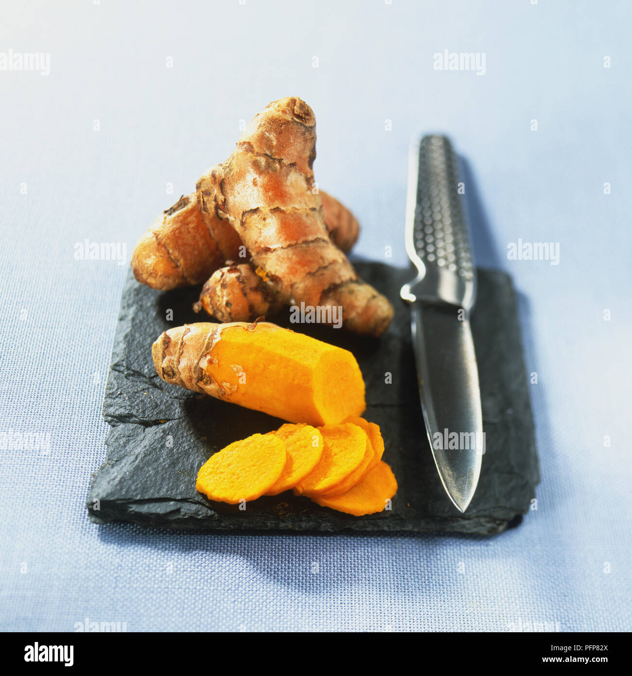 Curcuma longa, two fresh Turmeric rhizomes on slate tile with metal ...