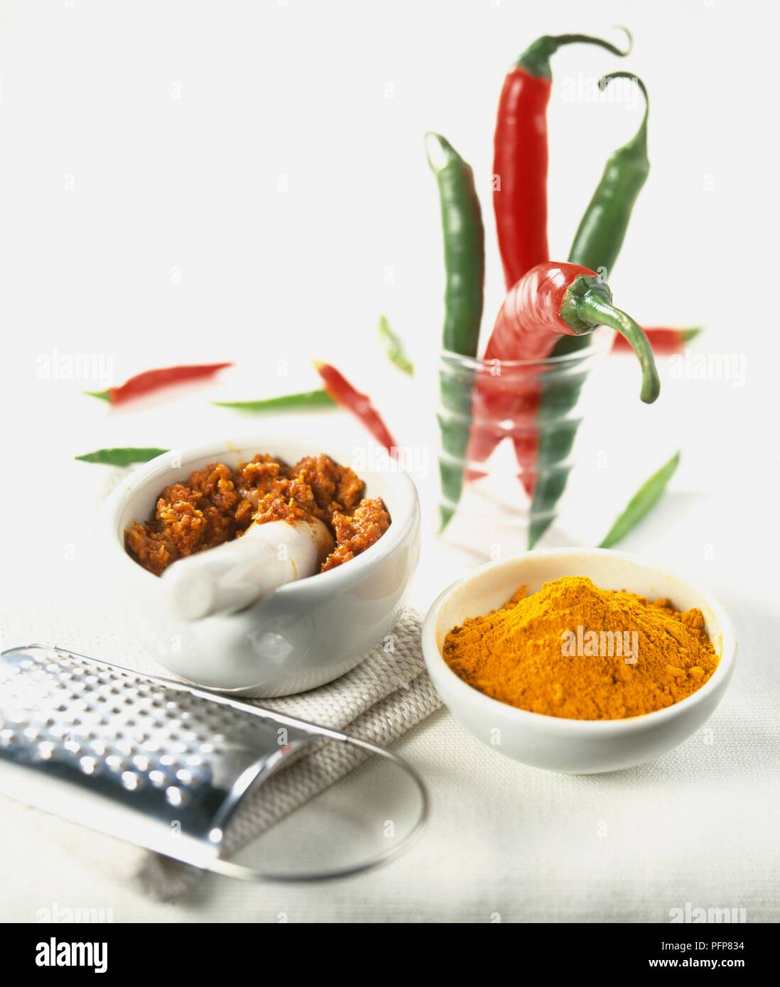 Ground turmeric, crushed spices in mortar, and whole green and red ...