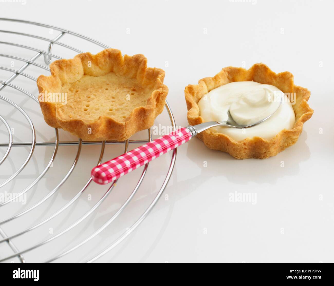 Cream and spoon in baked pastry shell and pastry shell on wire rack ...