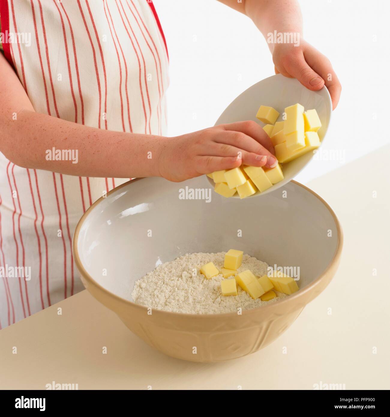 Girl using hands to add butter from white bowl on top of flour in ...