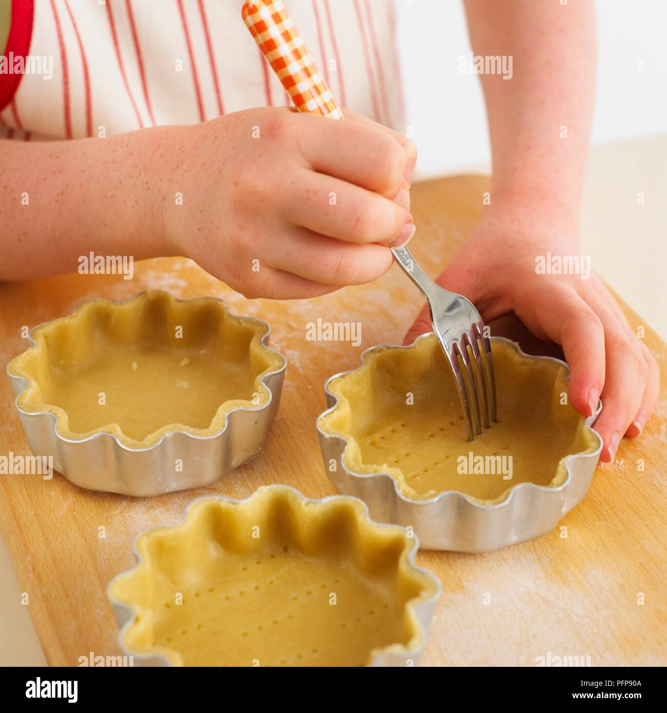 Girl using fork to make holes in pastry base inside cake tin Stock ...