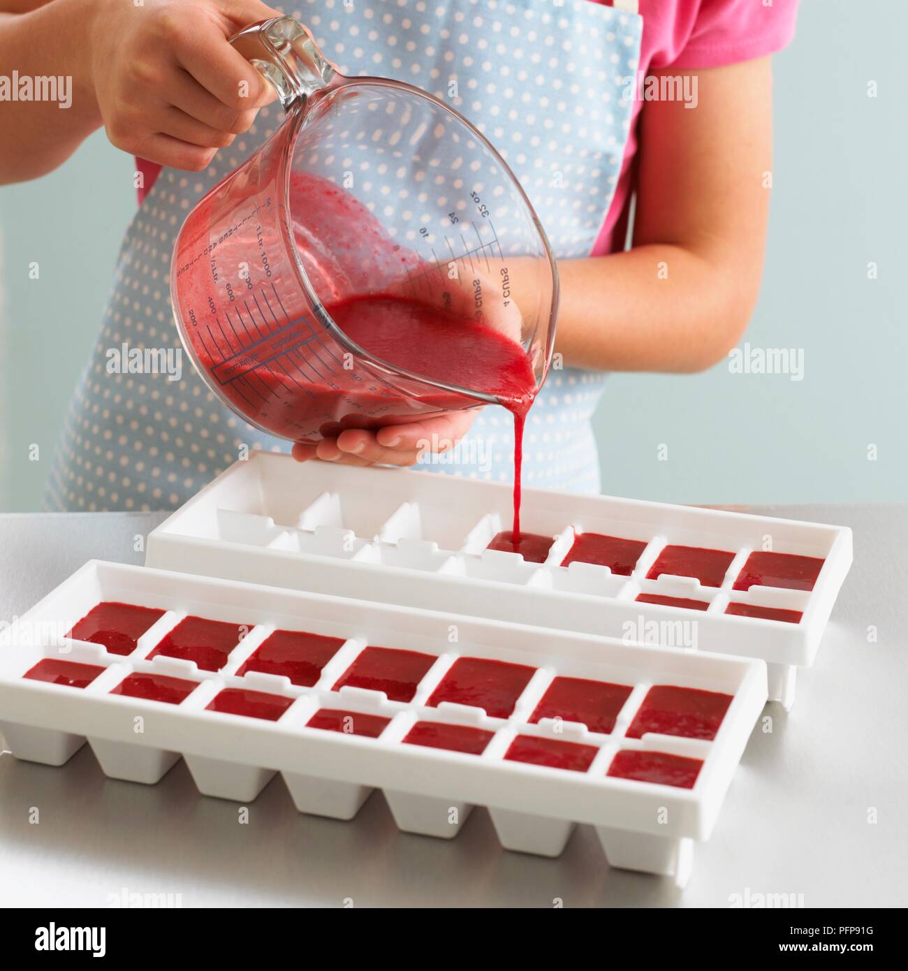 Girl pouring fresh raspberry juice into ice cube trays Stock Photo - Alamy