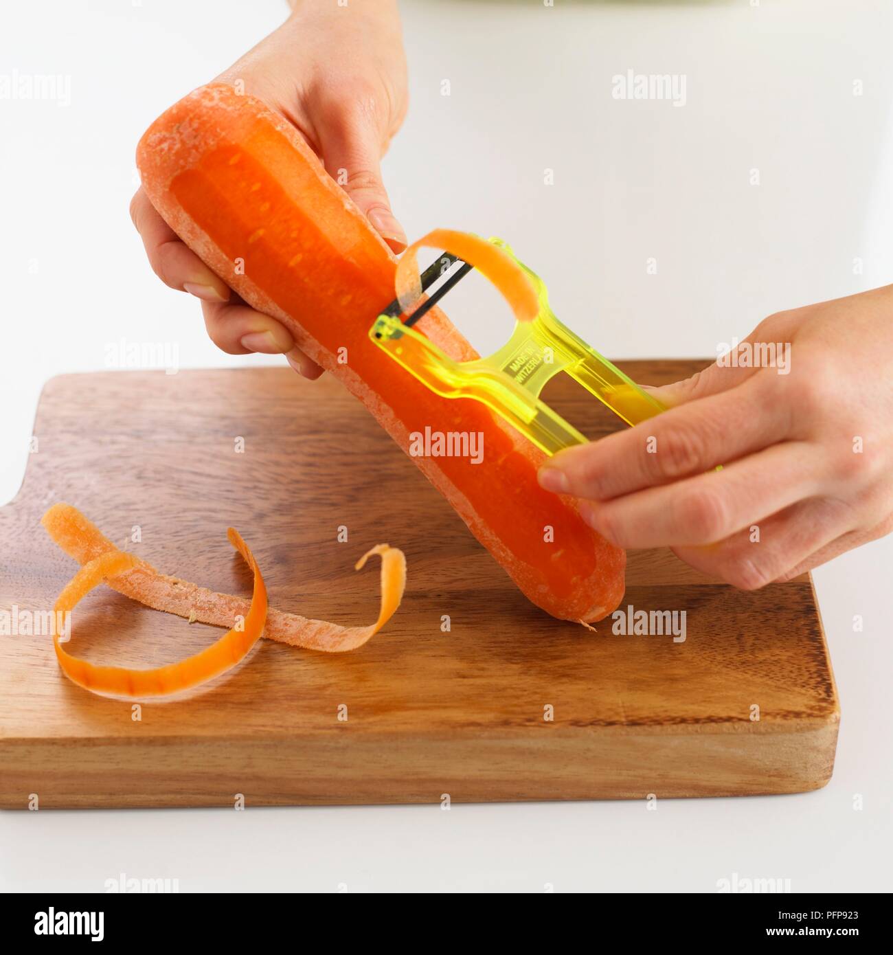 Boy using peeler to peel carrot on wooden chopping board Stock Photo ...
