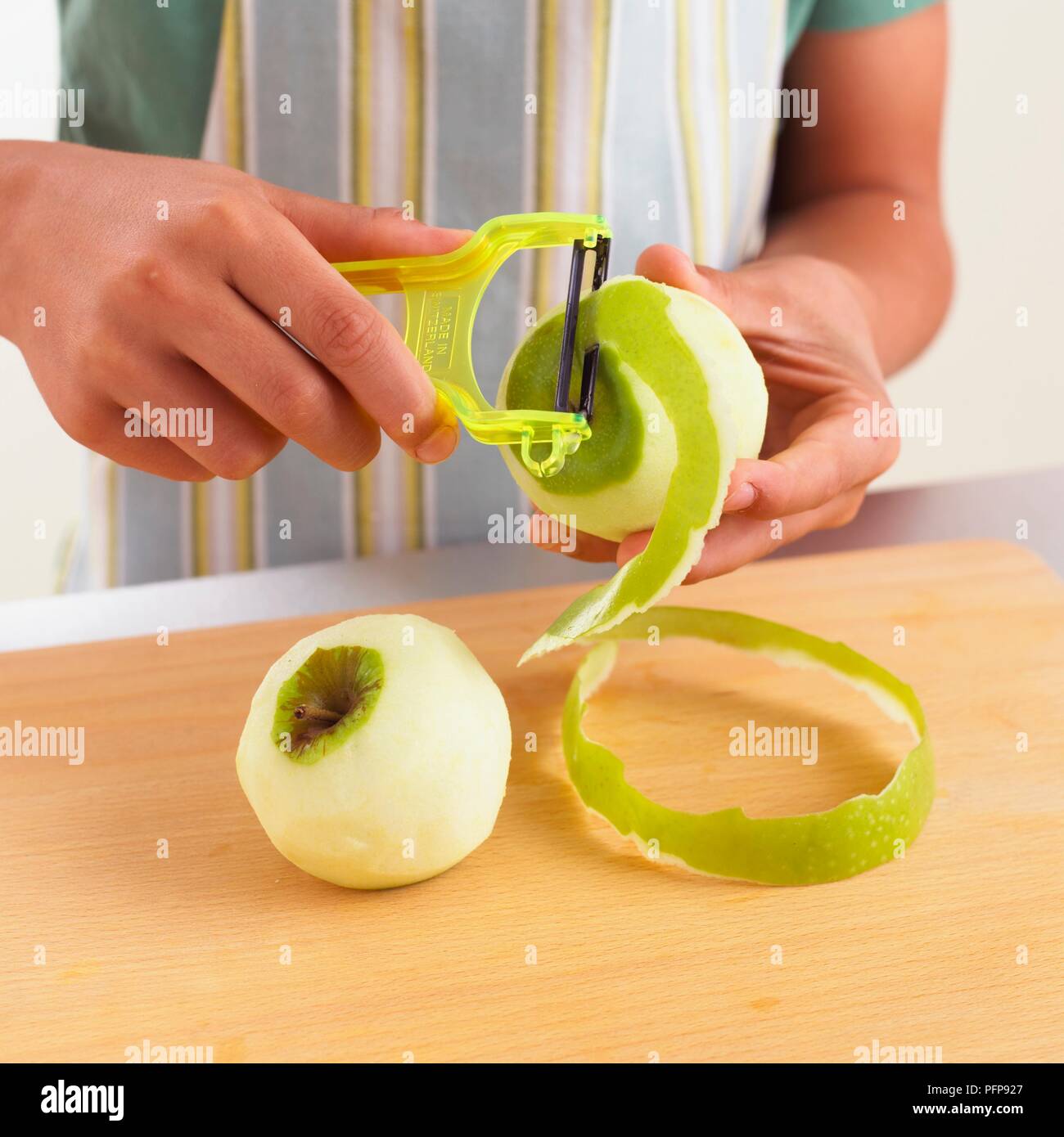 Boy using peeler to remove peel in spiral from green apple Stock Photo ...