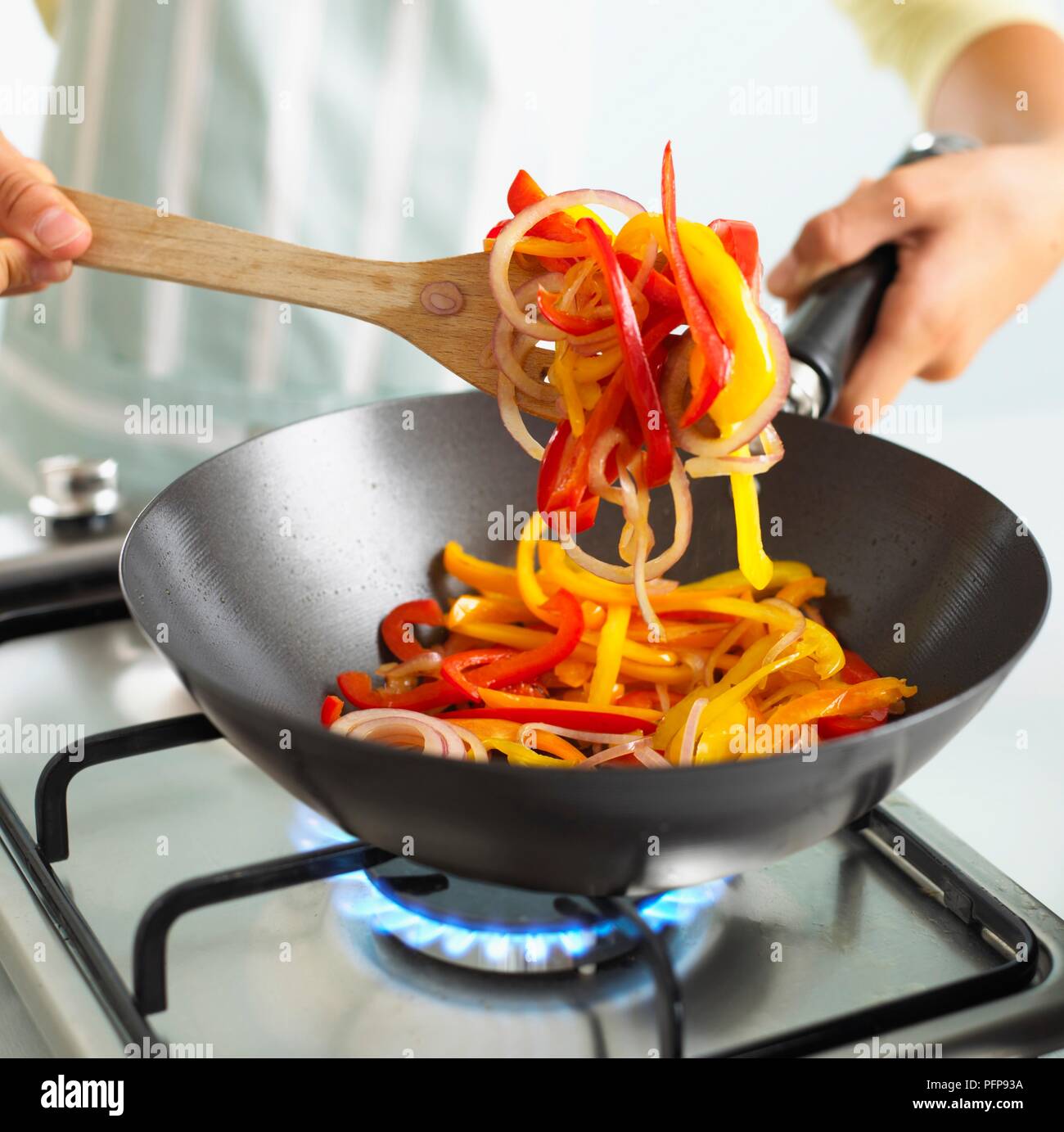 Child stirring sliced bell peppers and onions in frying pan using ...