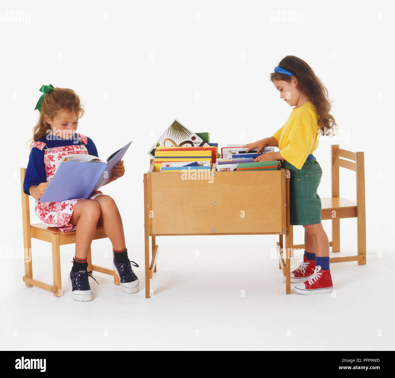 Girl sorting through books and folders, second girl sitting on chair ...