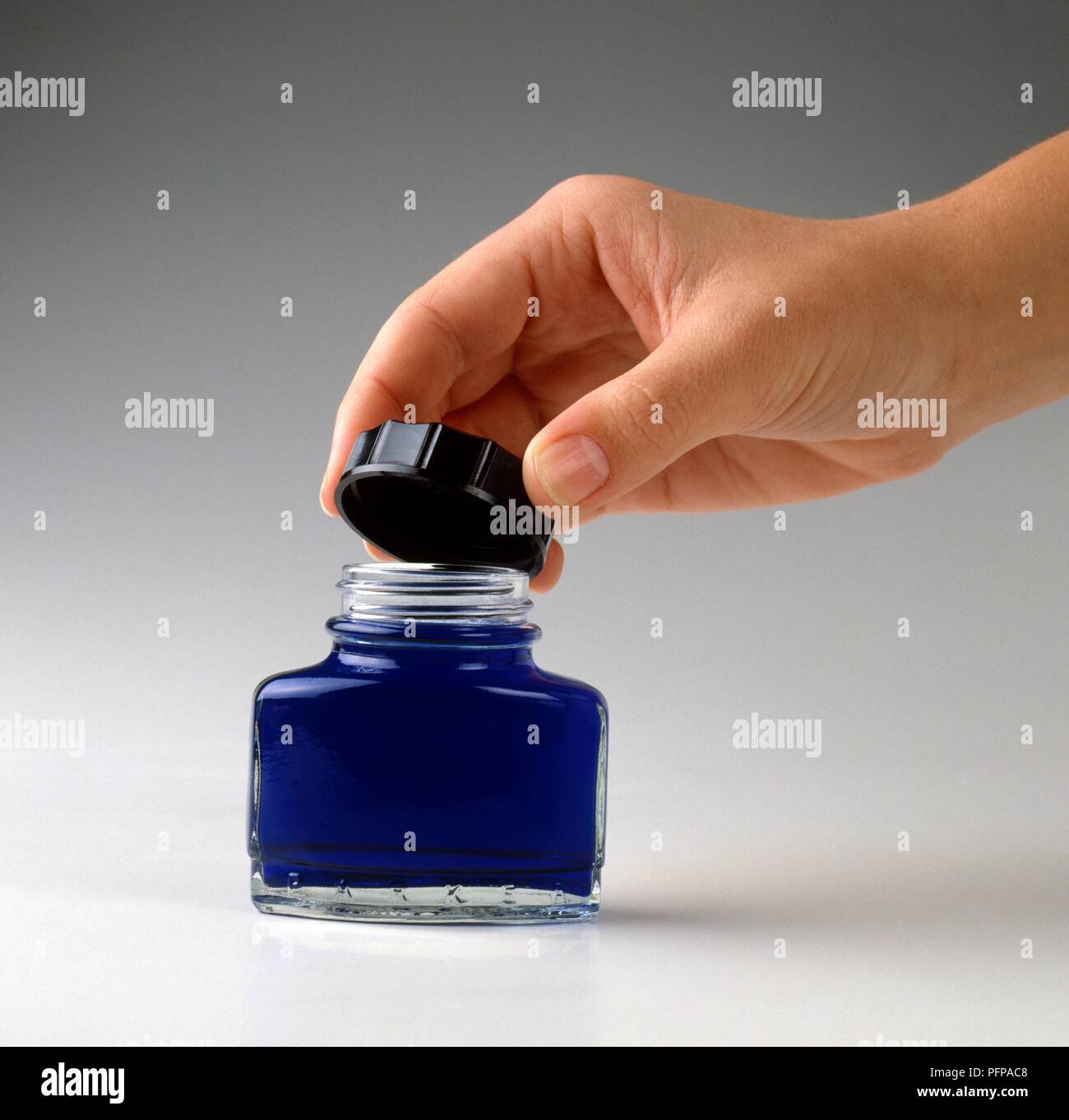 Hand holding cap above full bottle of blue ink Stock Photo - Alamy