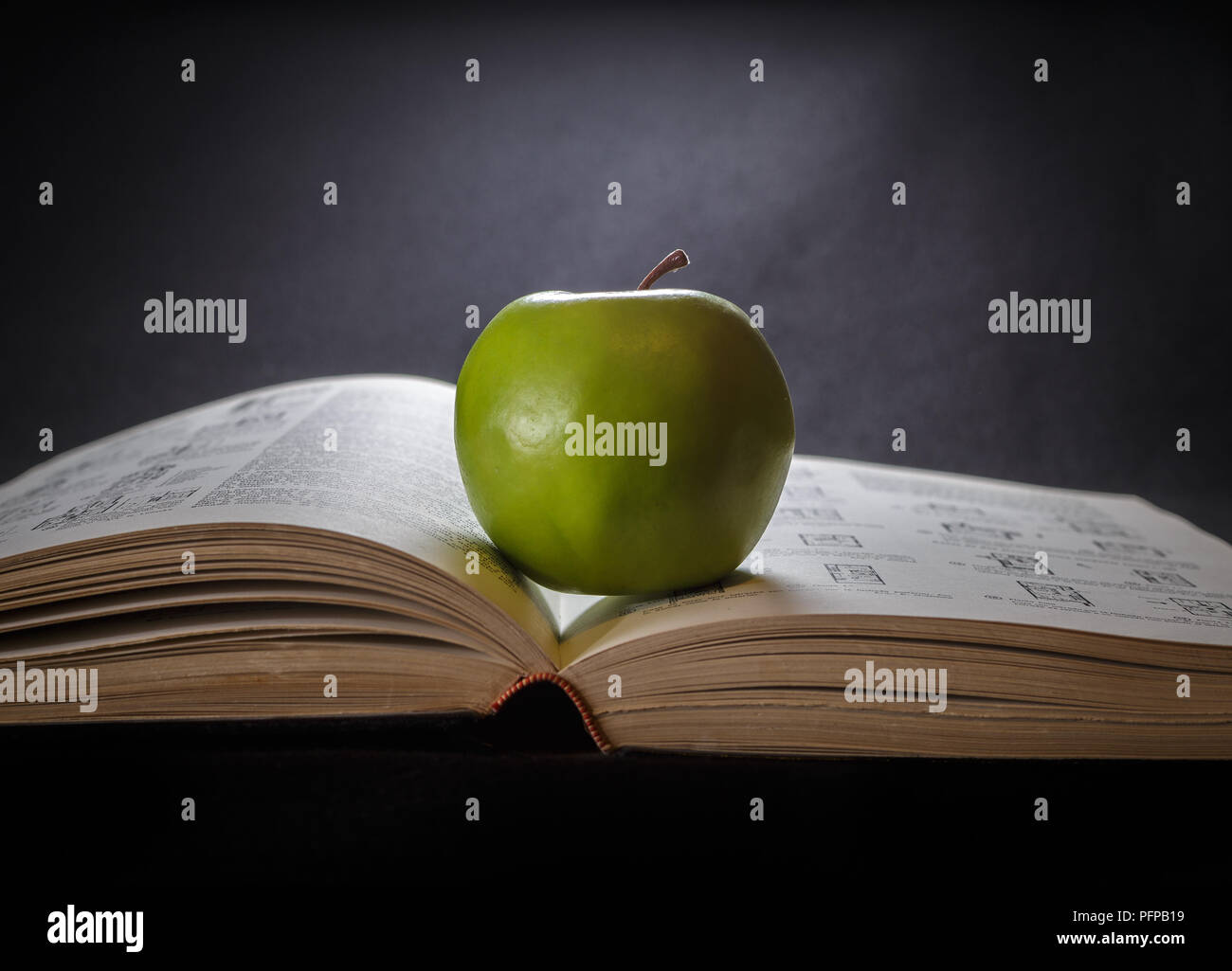 Green Apple on open book, black background Stock Photo - Alamy