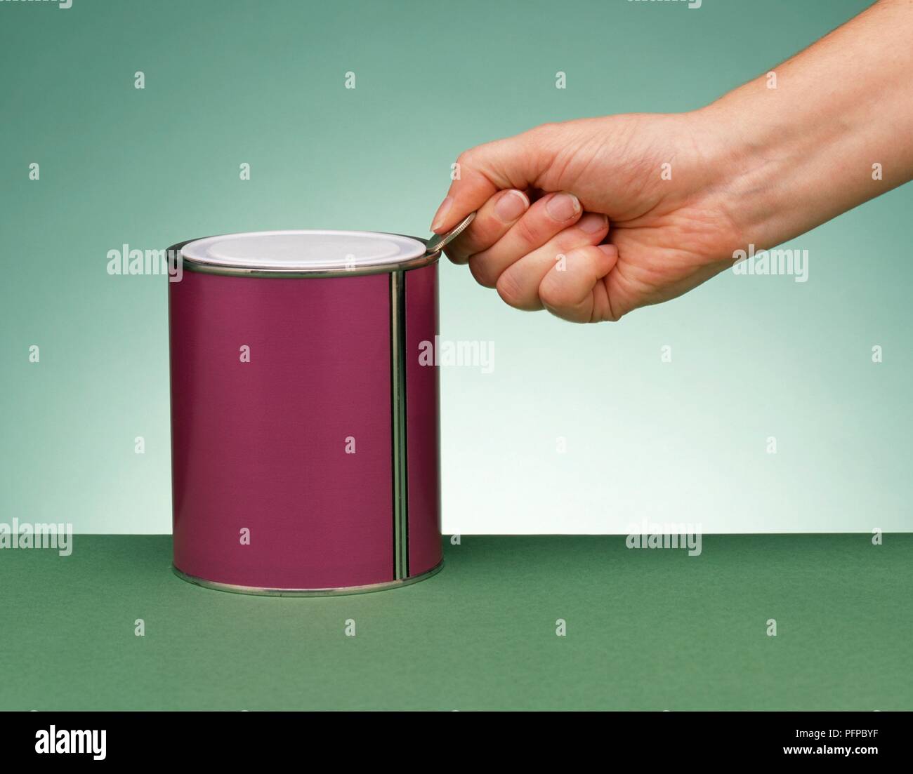 Hand attempting to lever a paint pot lid open with a coin, close-up ...
