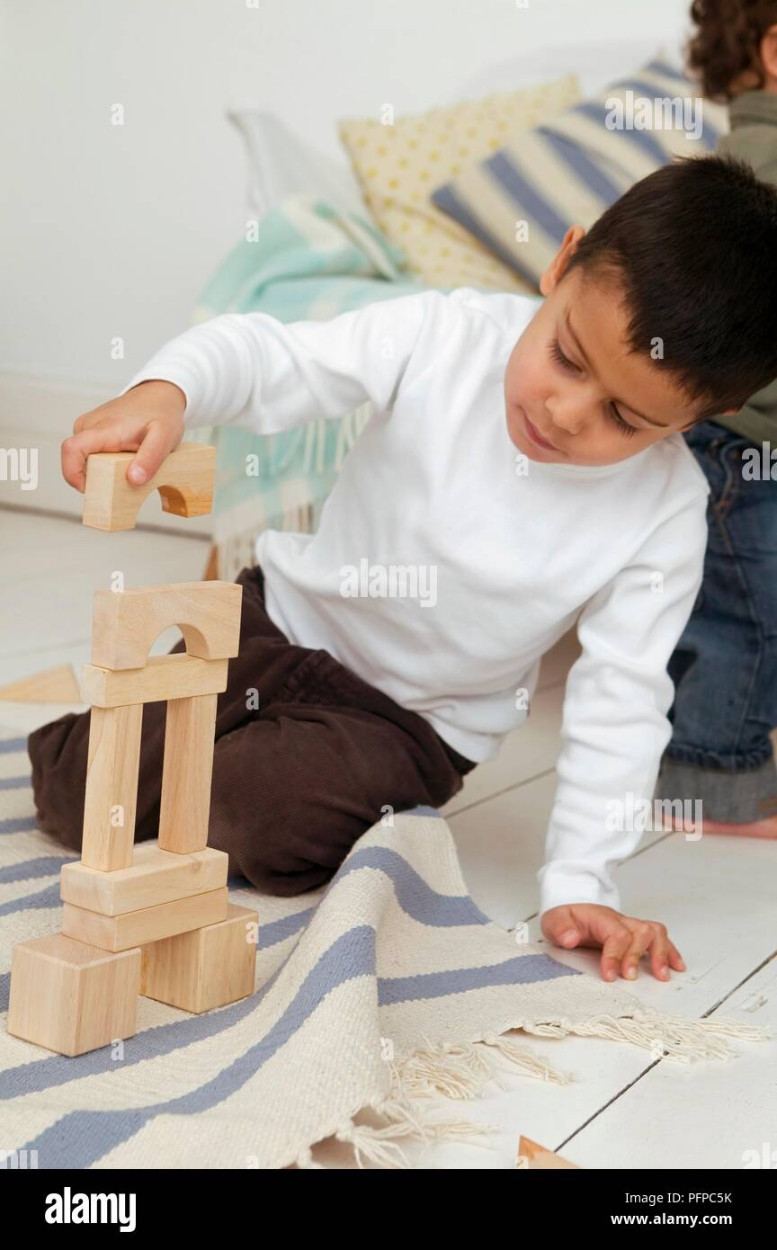 Boy sitting on floor stacking wooden blocks Stock Photo - Alamy