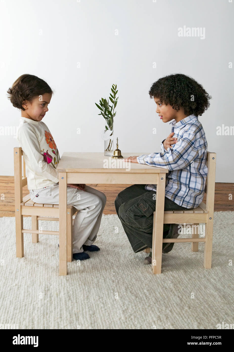 Five year old girl and boy sitting opposite each other at peace table ...