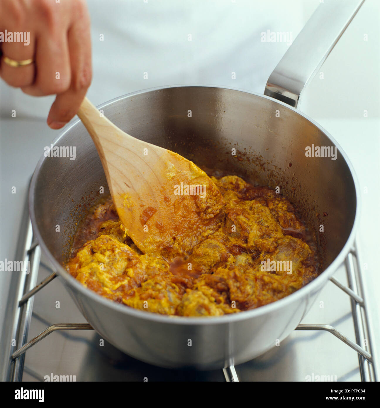 Using wooden spoon to stir Bhuna Gosht lamb marinated in yoghurt and ...