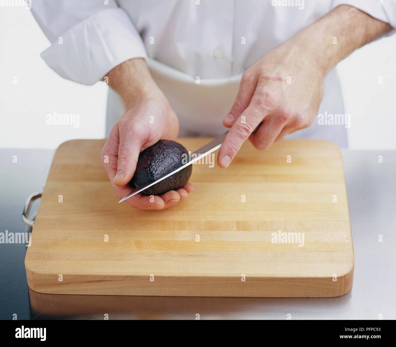 Chef using kitchen knife to slice whole avocado above wood chopping ...