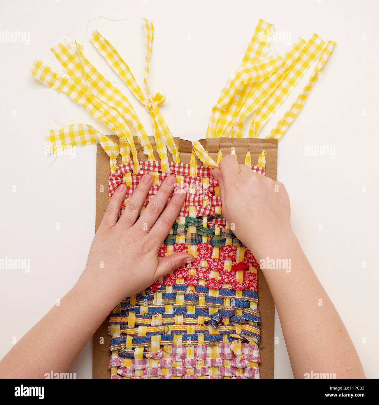 Girl's hands weaving strips of colourful fabrics into rag mat, close-up ...