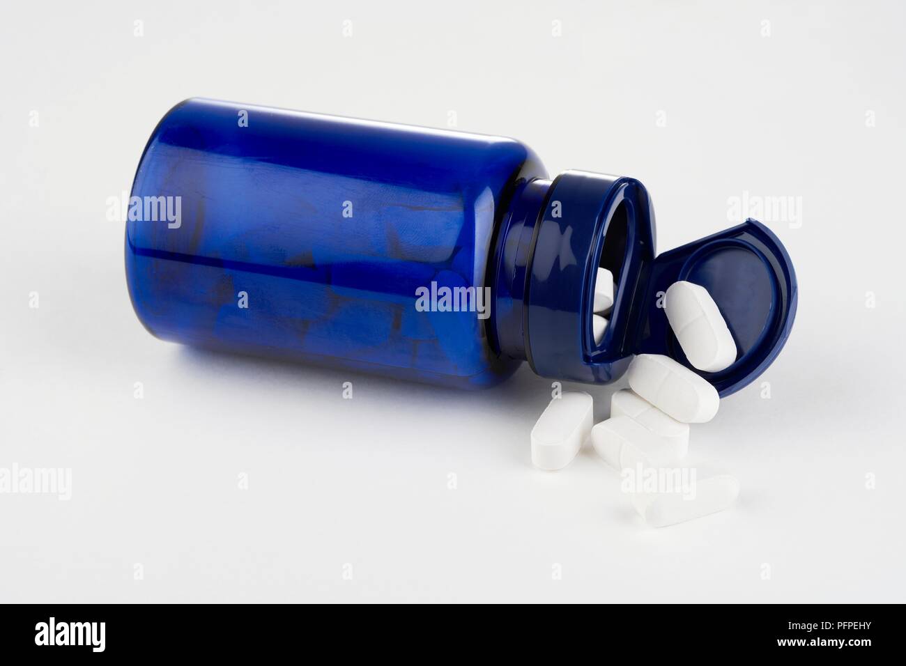 Calcium pills spilling from blue bottle lying on side Stock Photo - Alamy