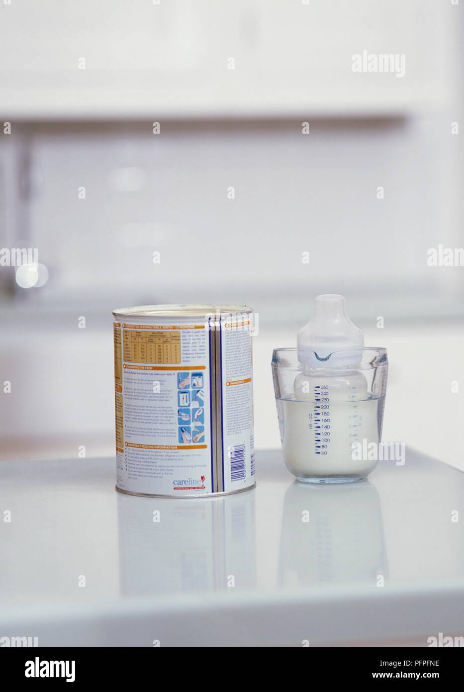 Tin of powdered milk next to baby feeding bottle in glass measuring jug ...