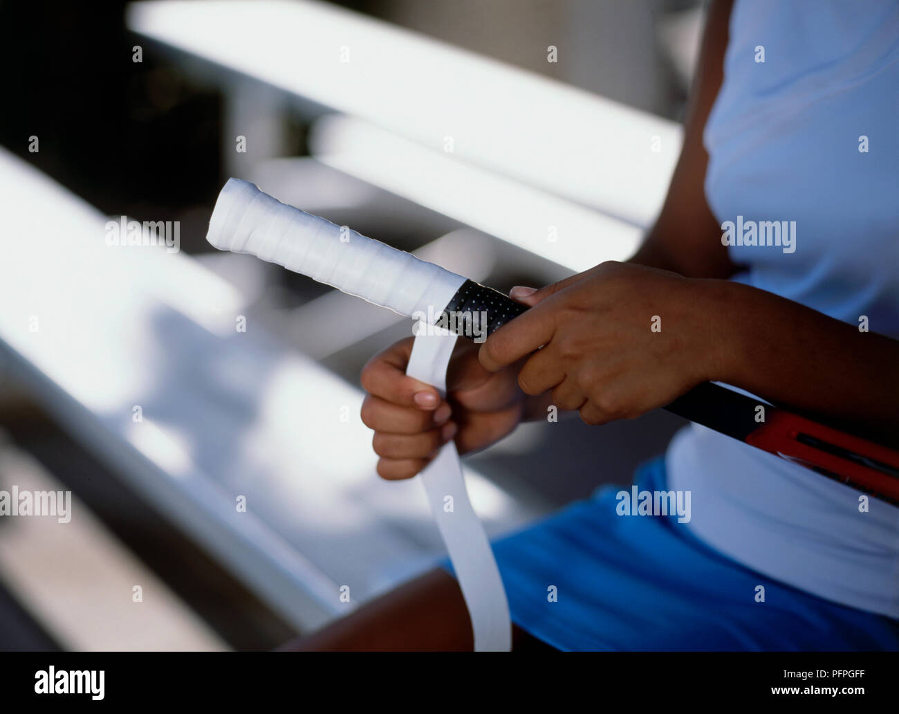 Teenage girl wrapping white tape around tennis racquet handle, close-up ...