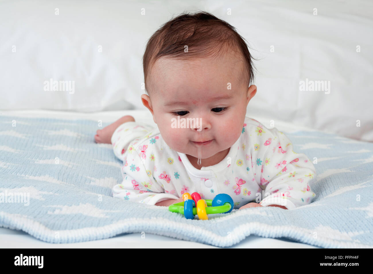 Baby girl lying on front on blue blanket on bed drooling looking at ...