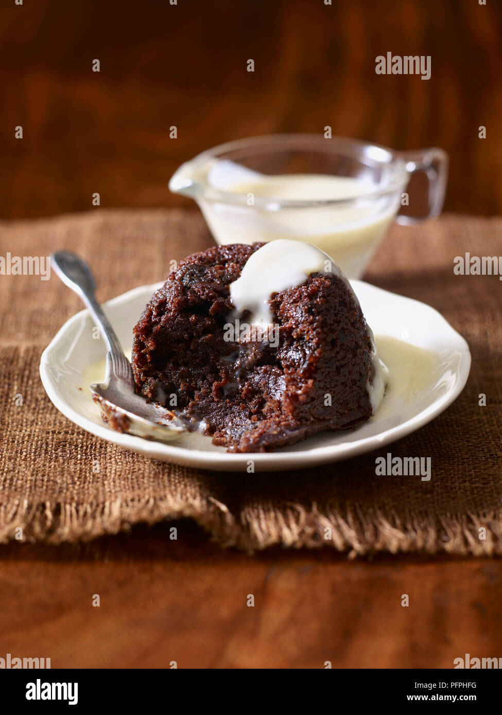 Chocolate and prune sponge pudding served in bowl with jug of brandy ...