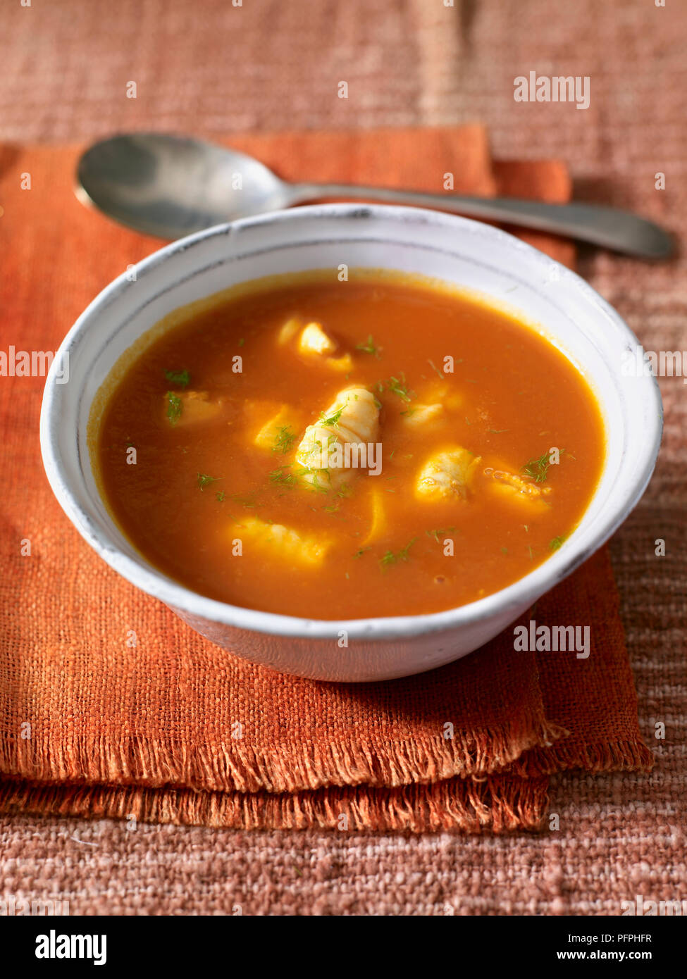 Rich haddock and monkfish soup served in bowl on napkin and spoon on ...