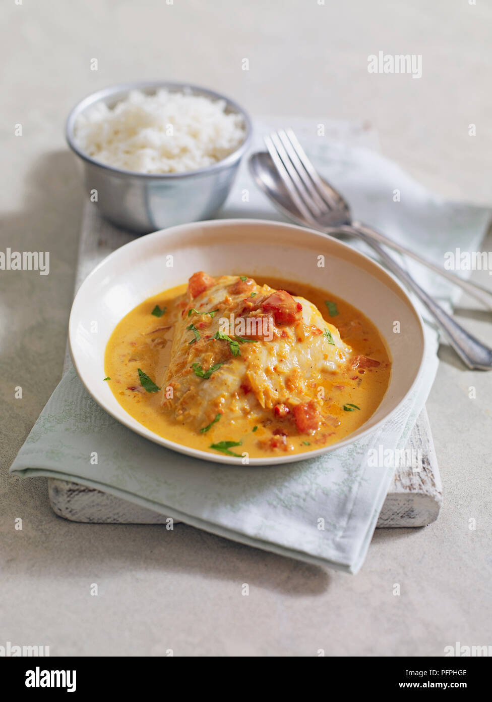 Thai red snapper curry served with bowl of basmati rice, cutlery, and ...