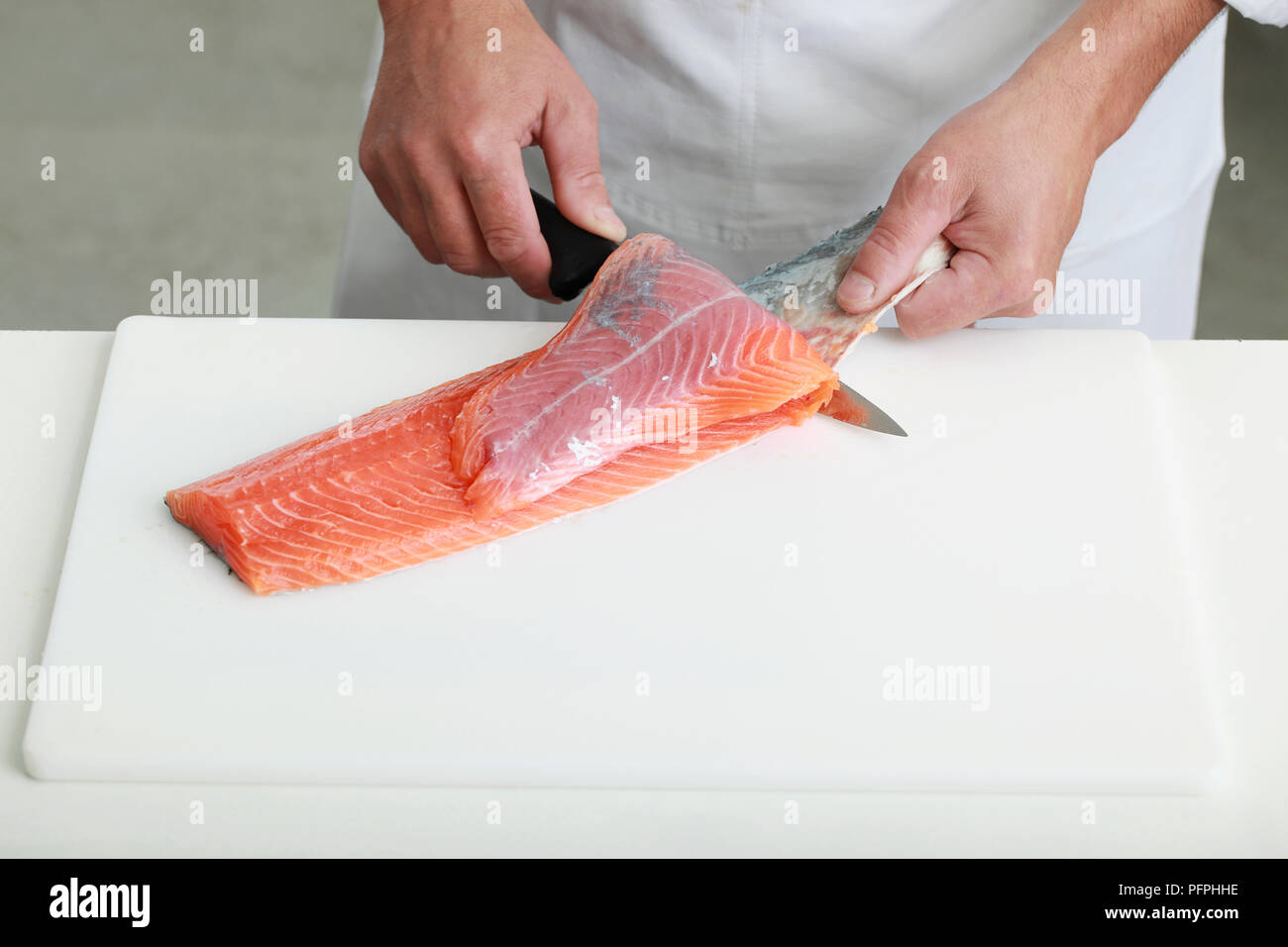 Skinning a salmon fillet, making a cut between the flesh and skin at ...